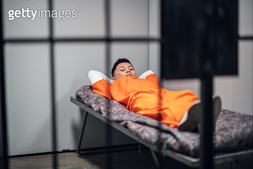 A prisoner in an asian high-security prison lies on a bunk in a red ...
