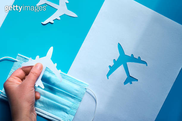 Restart flying, end quarantine. Hand holding paper plane over face mask ...