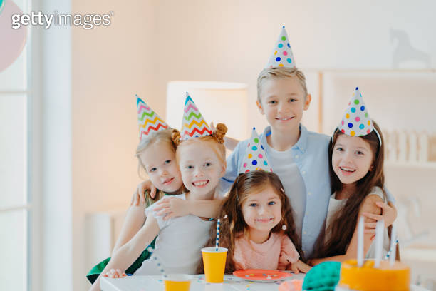 Group of adorable kids wear party hats, embrace and have fun, celebrate ...