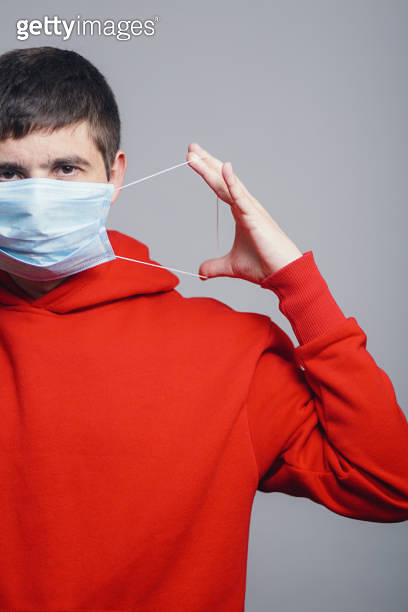Portrait of serious young pulled gum on medical mask on face on gray ...