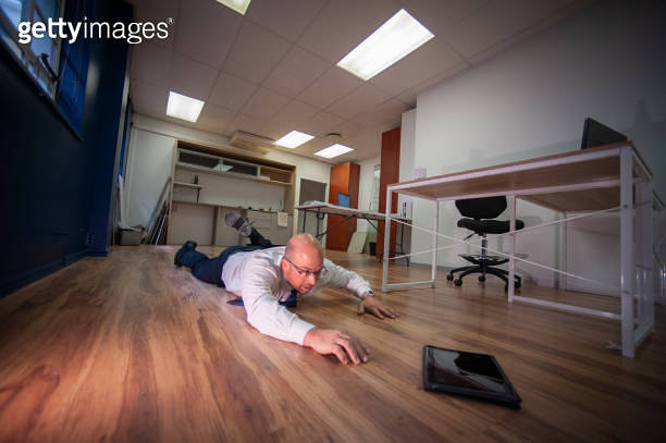Man falling flat on trhe ground and drops a digital tablet in an office ...