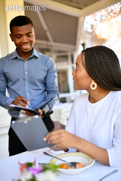 Waiter taking food order from Young woman on restaurant porch in summer ...