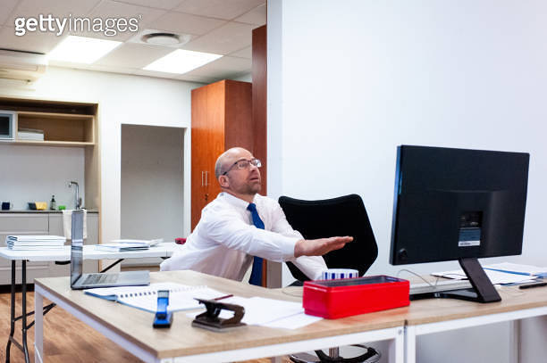 Goofy office employee standing looking at screen as his hand slips and ...