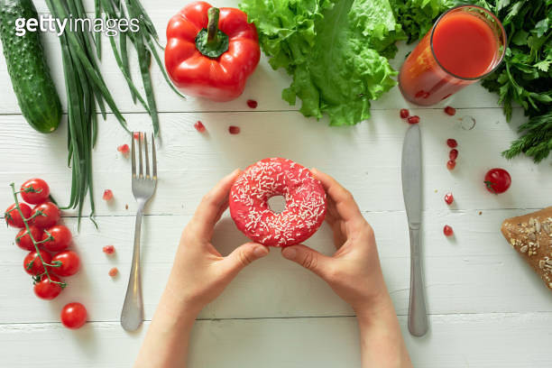 Female hands hold a tasty donut on a background of vegetables. The ...