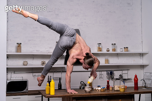 Muscular man stand on one the hand in the kitchen and holding bottle ...
