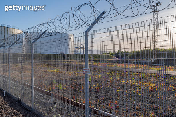Steel fence, topped with razor wire, protecting a fuel storage facility ...