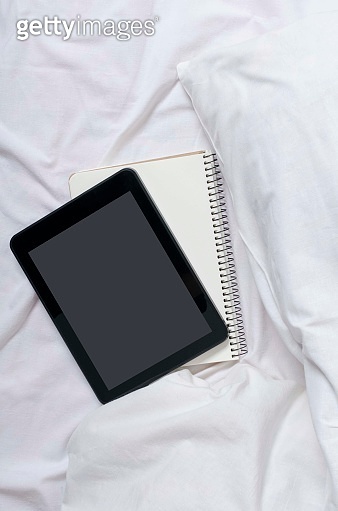 Top view of device with blank screen and notebook on the white linens ...