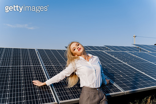 Woman leans on solar panels. Blonde dressed white formal shirt on the ...