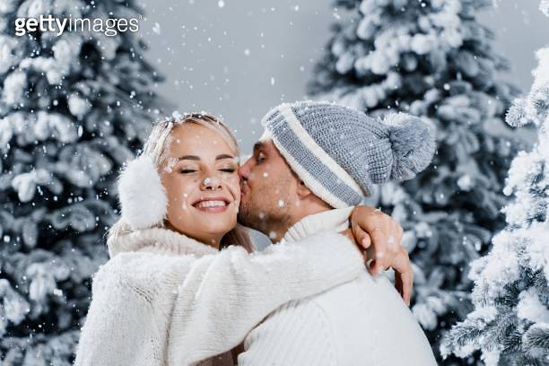 Falling snow and kisses. Happy young couple close-up hugs and kiss near ...