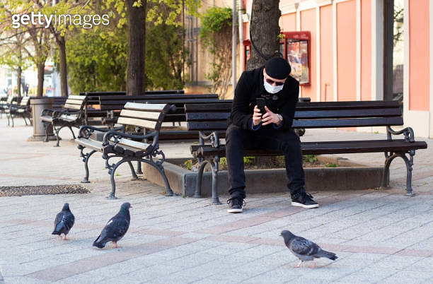 Young man with protective mask and sunglasses sitting alone on empty ...