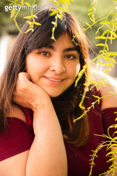 portrait of hispanic woman at sunset surrounded by green tree branches ...