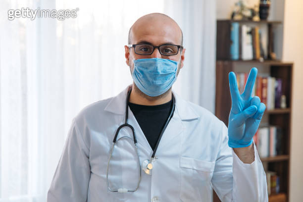 Portrait of a young male doctor making victory sign in medical mask ...