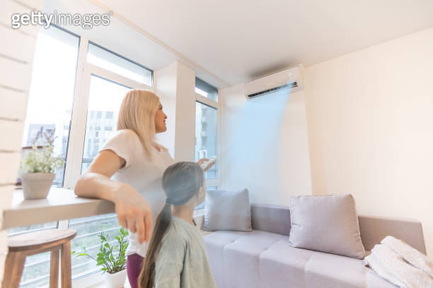 Happy family under air conditioner, mom holding remote control switch on conditioning in living ...
