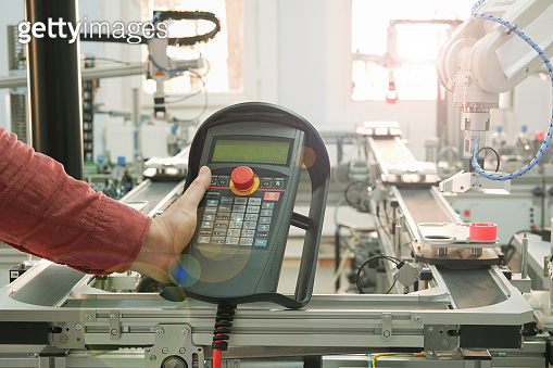 Close up of man's hand holding teach panel to control robot arm which is integrated on smart ...