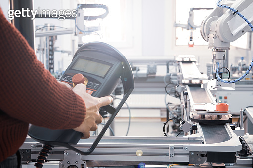 Close up of man's hand holding teach panel to control robot arm which ...