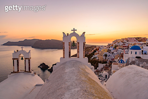 Blue domed churches and bell tower facing Aegean Sea with warm sunset ...