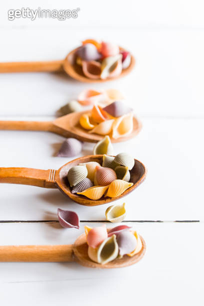 Colorful conchiglie pasta shells on wooden spoons with white wooden ...