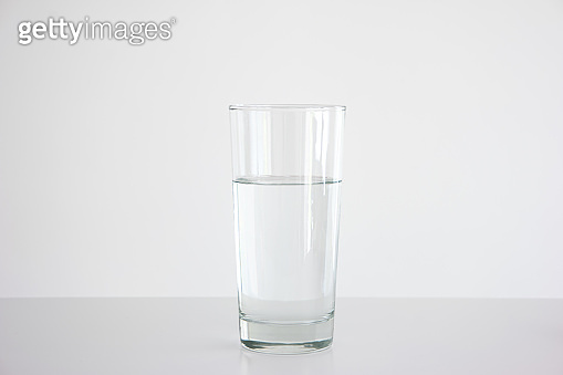Clear glass three quarters full of water set on white table isolated ...