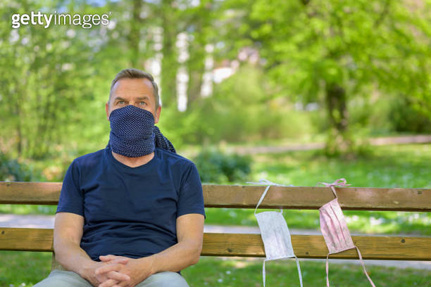 Man wearing a face guard seated on a park bench (1218924322) - 게티이미지뱅크