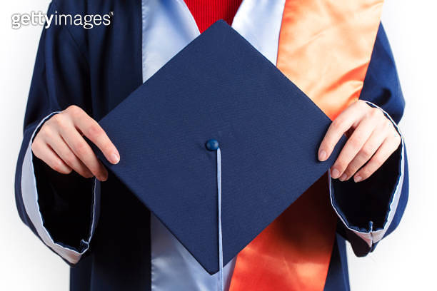 Hands holding graduation cap. In the background, the young female ...