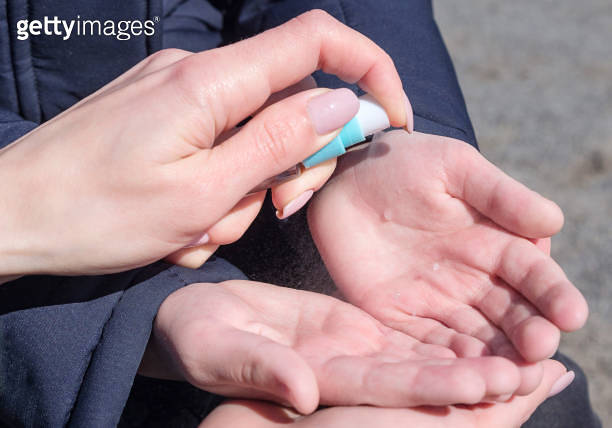 A woman sprays an antibacterial disinfectant spray on the hands of a ...