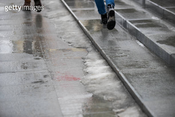 Walk on wet melted ice pavement. Back view on the feet of a man walking ...