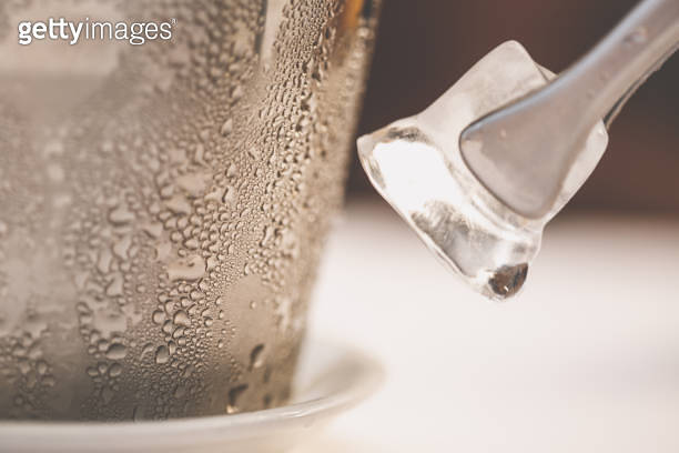 Cut out shot of sweaty ice bucket and serving tongs holding an ice cube ...
