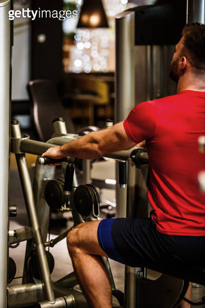 Muscular male athlete using exercise machine to do his strength ...