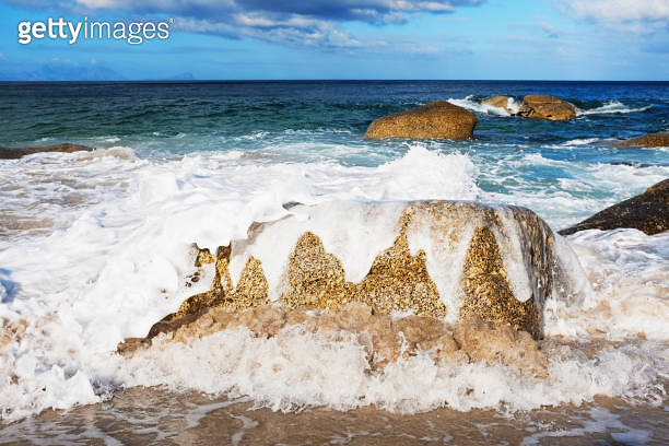 Surf breaks over a rock on a beautiful sunny shore, resembling icing on ...