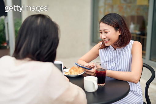 Two young women having coffee break together use smart phone. Happy ...