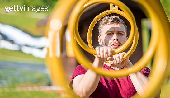 Portrait of fit man overcomes hanging rings obstacles at the extreme ...
