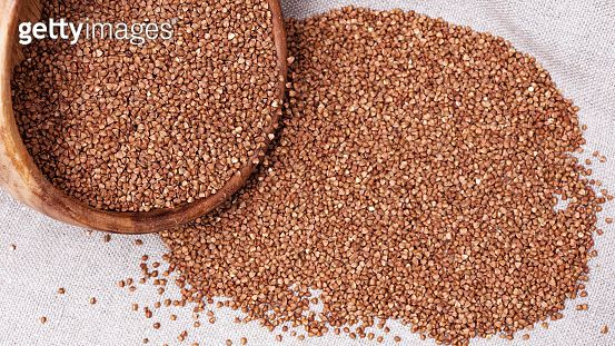 Raw roasted buckwheats from round wooden bowl pour on cloth surface ...