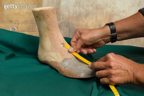hands of a orthopedic shoemaker are measuring a wooden last for quality ...