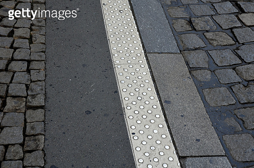 on the edge of the sidewalk is a white safety line with bumps ...