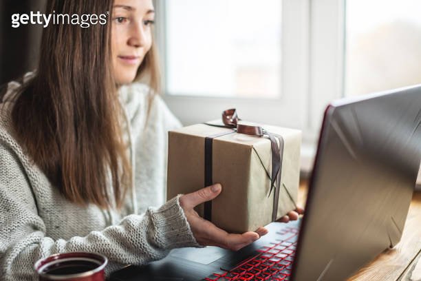 Woman in a sweater is sitting in front of a computer screen with a gift ...