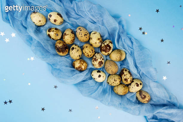 Many Quail eggs, textile with sparkle confetti on light blue background ...