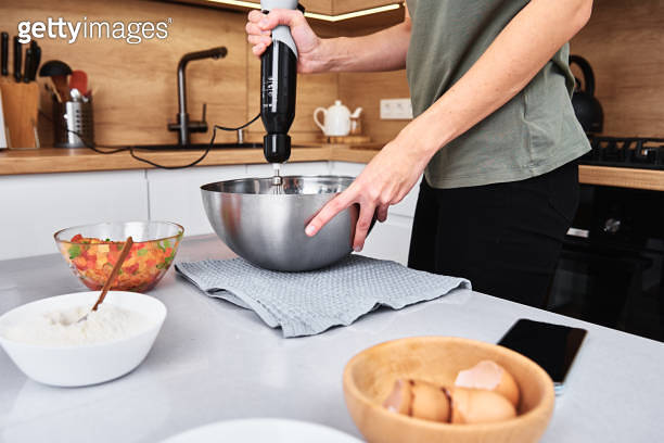 Woman in kitchen cooking a cake. Hands beat the dough with an electric ...