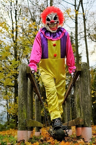 Halloween. Evil clown in overalls and in a scary mask on the playground ...