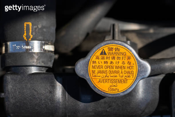 Orange radiator cap with warning labels in different languages: never ...