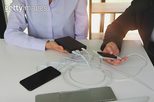Two people using two mobile phone sharing USB Power Bank on a table to ...