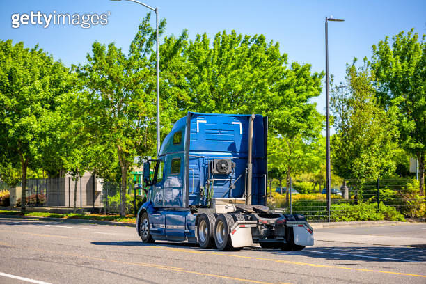 Blue big rig semi truck tractor running on the green city street road ...