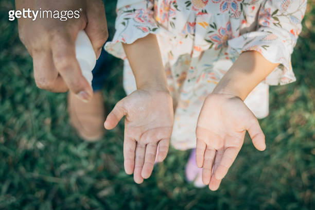 Mother squeezing hand sanitizer into little daughter's hand outdoors ...