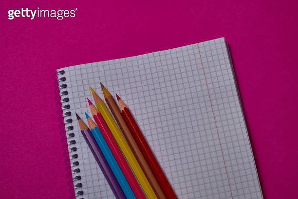 Multi colored crayons and binder notepad at magenta background with ...