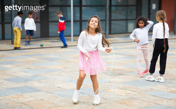 Tween girl in pink skirt jumping rope in schoolyard during recess ...