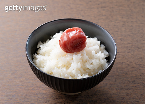 Japanese pickled plums and freshly cooked rice set against a wooden ...