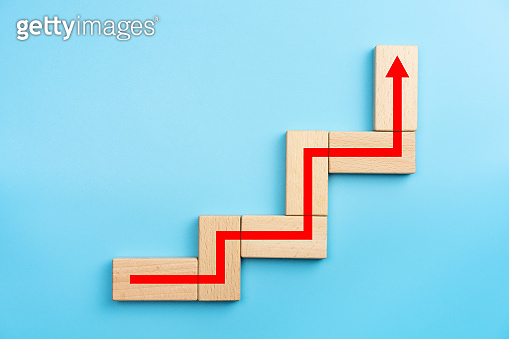 Wooden blocks stacking as step stair with red arrow up, blue background ...