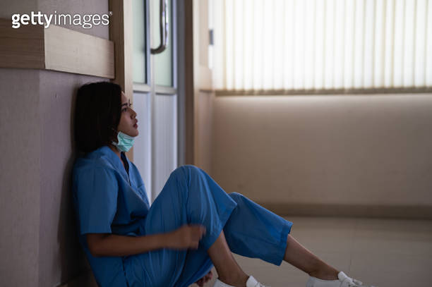 Young Asian woman nurse looking distraught and sad sitting on the floor ...