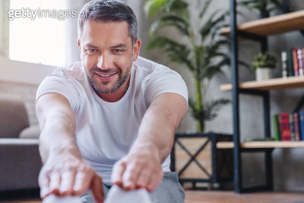 Close up of handsome adult sporty man stretching his legs at home 이미지 ...
