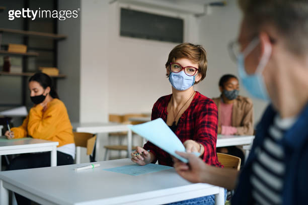 Young students with face masks at desks at college or university ...