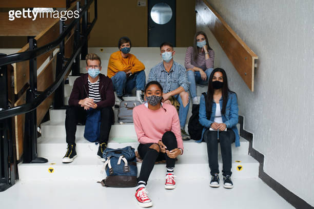 Front view of young students with face masks back at college or ...